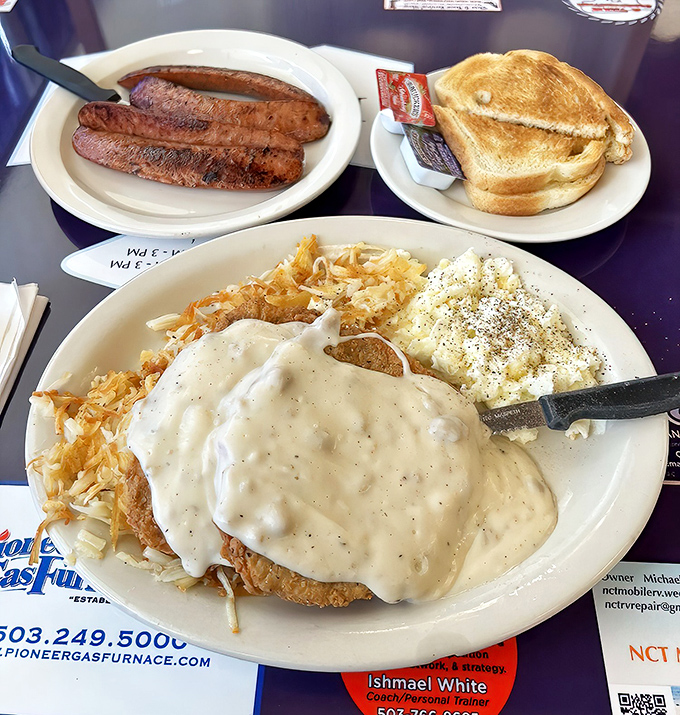 Behold the chicken fried steak in its natural habitat – swimming in gravy, flanked by golden toast and sausage links standing guard.