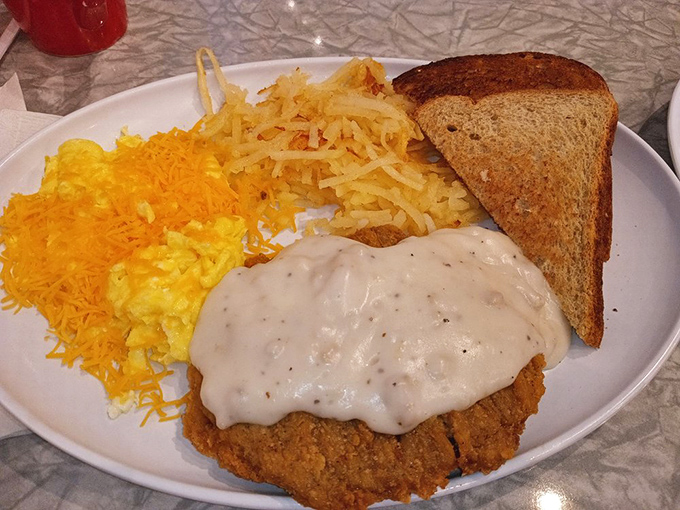 The famous country fried steak in all its glory – golden exterior, smothered in gravy, with eggs and hash browns standing by.