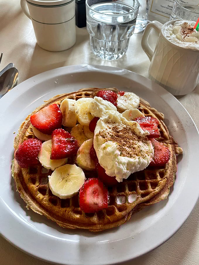 Breakfast nirvana achieved: a golden waffle crowned with fresh strawberries, bananas, and whipped cream that doesn't come from a can.