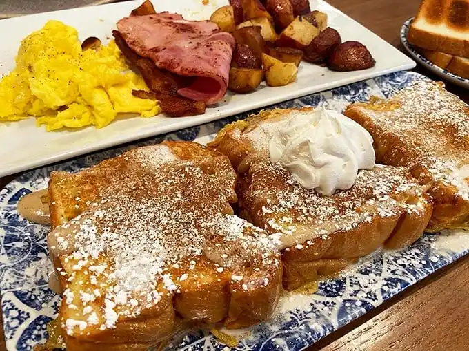 Breakfast that looks like it belongs on a magazine cover – golden French toast with ham and home fries that turn morning hunger into culinary excitement.