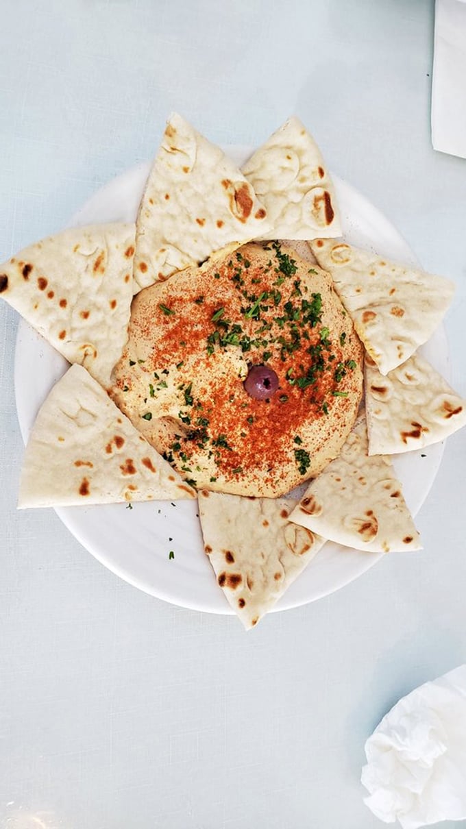 Hummus arranged like a sunburst with pita points standing ready—a simple appetizer elevated to art form status.