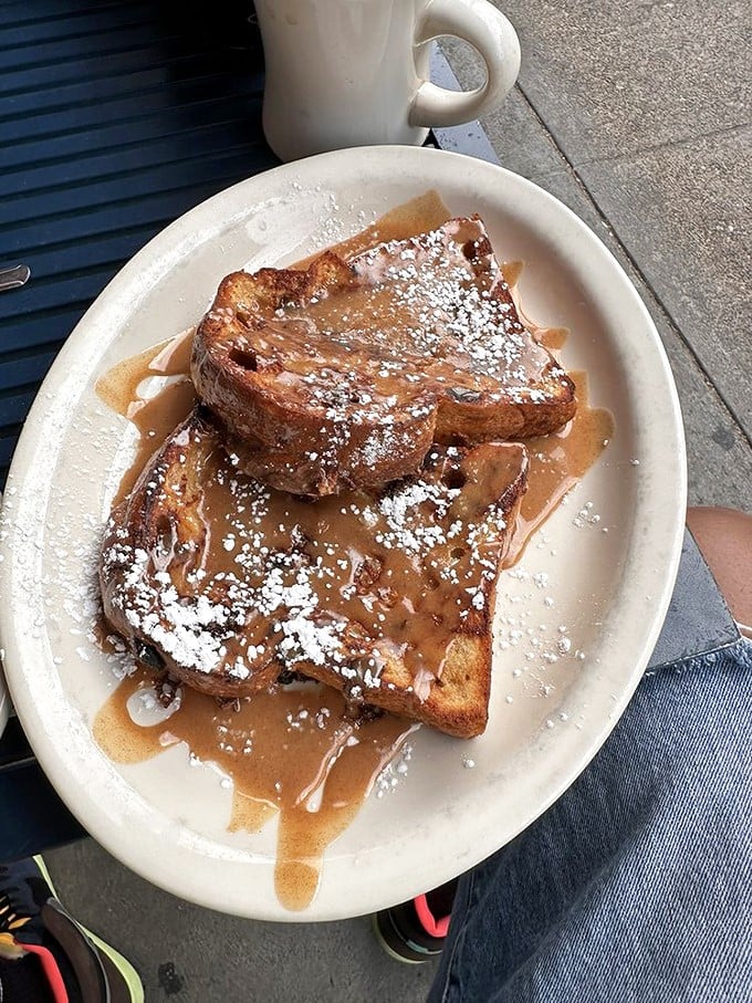 French toast that's achieved breakfast nirvana – thick-cut, perfectly caramelized, and dripping with maple syrup and powdered sugar confetti.