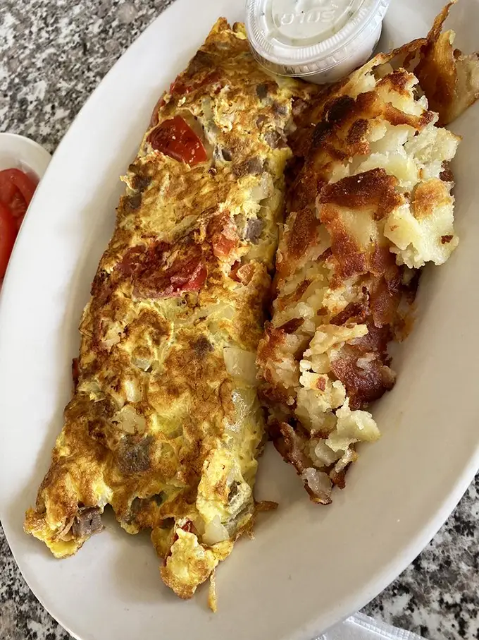 The Greek omelet arrives like a love letter from the Mediterranean—all folded eggs, bright tomatoes, and savory satisfaction.