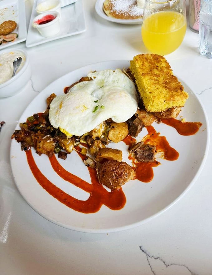 Breakfast architecture at its finest – layers of flavor built on a foundation of potatoes, crowned with eggs and artistic sauce flourishes.
