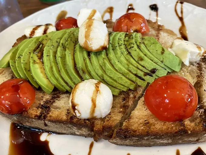 Avocado toast elevated from millennial cliché to breakfast masterpiece with perfectly fanned slices and bursts of roasted tomato flavor.
