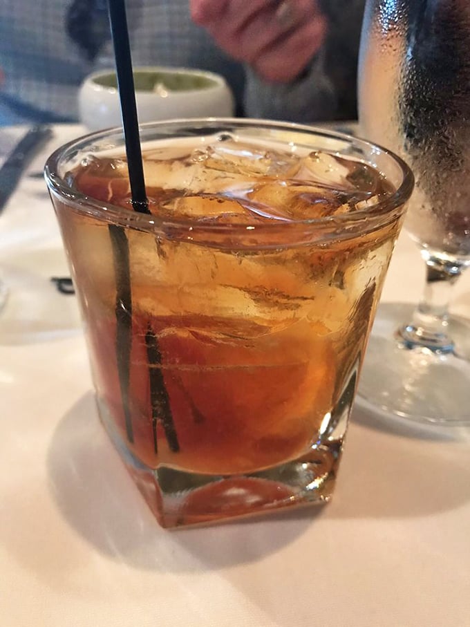 An old fashioned cocktail sits regally on white linen—amber liquid and ice in perfect harmony, waiting to complement whatever French delicacy comes next.