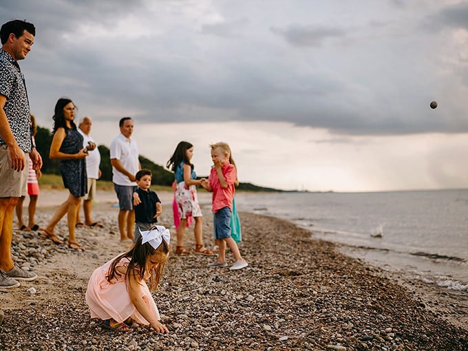 Family memories being written in stone and sand. Generations gather at the shoreline, proving that the simplest pleasures—skipping rocks and collecting shells—remain timeless.