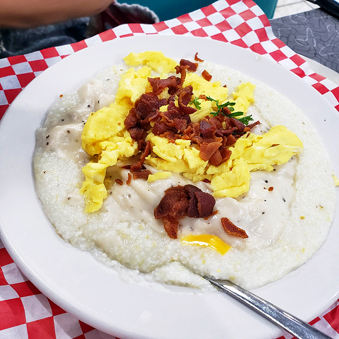 Southern comfort in a bowl: creamy grits crowned with scrambled eggs and crispy bacon bits—proof that simplicity sometimes makes the most profound statements.