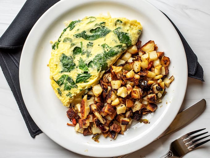 This isn't just any omelet—it's a fluffy yellow pillow stuffed with vibrant spinach, paired with potatoes crisped to golden perfection.