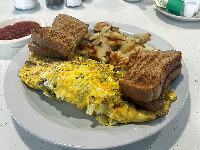 This isn't just an omelet – it's a fluffy yellow canvas painted with fillings, accompanied by toast standing at attention and hash browns crisped to golden perfection.