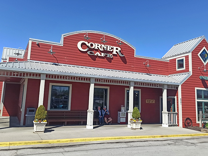 The red barn-like exterior of Corner Cafe stands proudly against the Missouri sky, complete with patriotic bunting and a welcoming porch that practically whispers, "Come on in, hungry traveler."