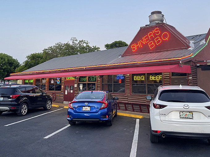 That neon sign isn't just advertising – it's a lighthouse for hungry souls. The log cabin exterior promises authentic barbecue without pretension.