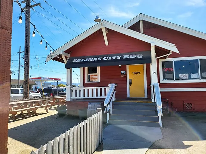 The little red house with the bright yellow door isn't trying to impress anyone—until you taste what's coming out of those smokers.