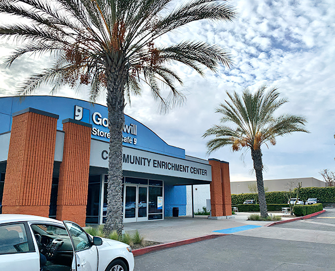 The blue-fronted Goodwill Southern California Community Enrichment Center stands ready to welcome bargain hunters beneath swaying palm trees, a treasure cave disguised as a retail store.