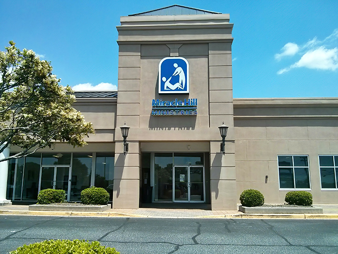 The iconic blue signage of Miracle Hill Thrift Store stands out against the beige building like a beacon for bargain hunters across Greenville.