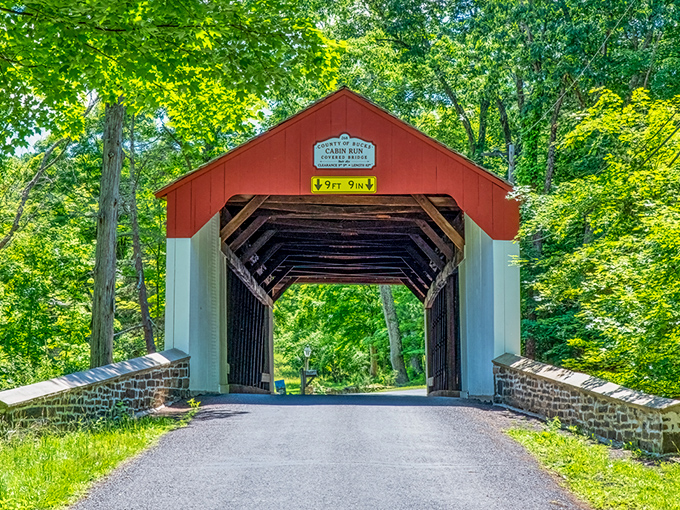 The classic red and white facade of Cabin Run Covered Bridge stands like a portal to the past, framed by autumn foliage and Pennsylvania's blue skies.