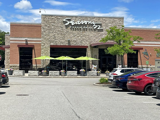 The stone facade of Seasons 52 stands like a culinary lighthouse, beckoning hungry travelers with its warm glow and those unmistakable bright green umbrellas.
