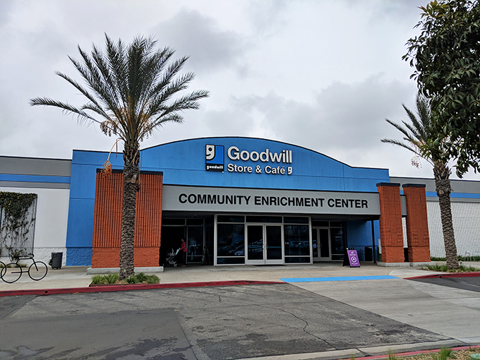 The blue-fronted Goodwill Southern California Community Enrichment Center stands ready to welcome bargain hunters beneath swaying palm trees, a treasure cave disguised as a retail store.
