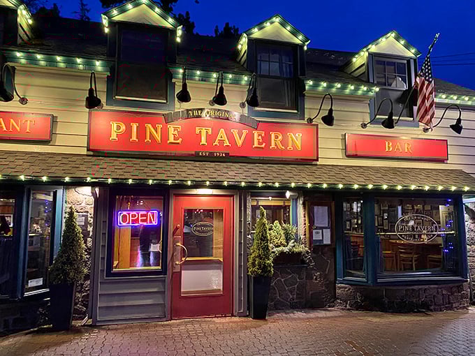 The charming exterior of Pine Tavern beckons with its classic red awning and stone facade, a timeless landmark in downtown Bend since the Great Depression era.