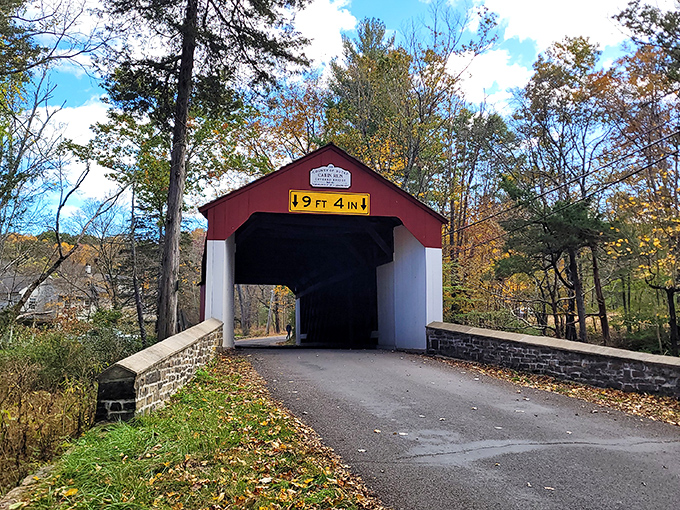 The classic red and white facade of Cabin Run Covered Bridge stands like a portal to the past, framed by autumn foliage and Pennsylvania's blue skies.