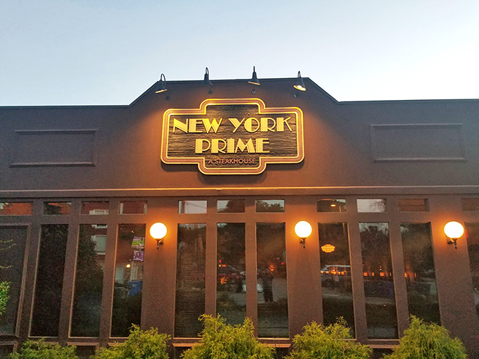 The neon glow of New York Prime beckons like a lighthouse for steak lovers—a humble exterior that belies the culinary treasures waiting inside.