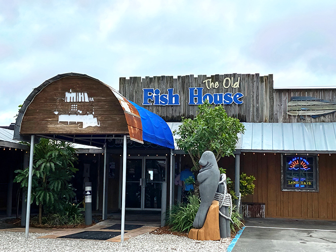 The weathered wooden exterior of The Old Fish House screams "authentic Florida" with its blue signage and that charming manatee statue standing guard at the entrance.