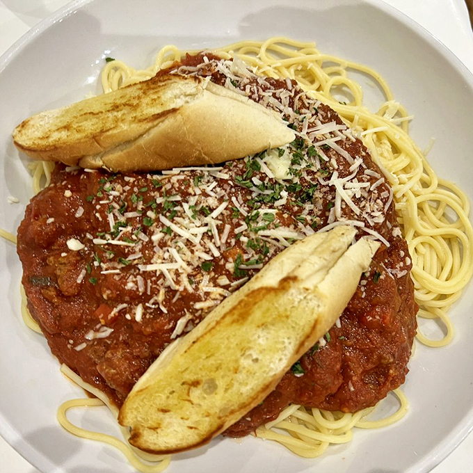 Spaghetti that would make nonna proud—al dente pasta swimming in robust sauce, topped with freshly grated cheese and garlic bread for essential sauce-sopping.