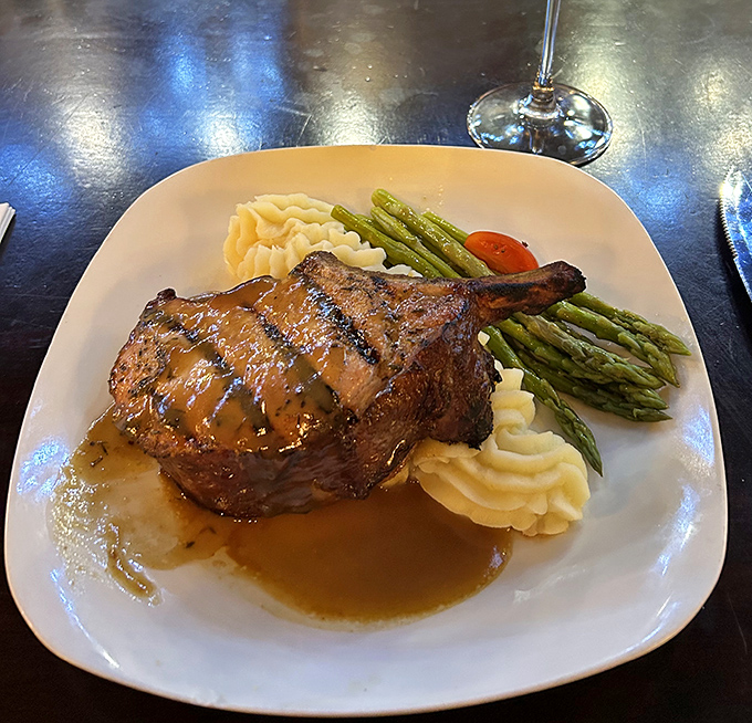 This isn't just a pork chop—it's meat architecture, perfectly balanced on a cloud of mashed potatoes with asparagus standing guard.