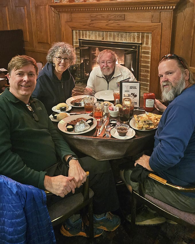 Happy diners gathered around a fireplace with loaded plates—this is what they mean by "breaking bread" in its most joyful form.