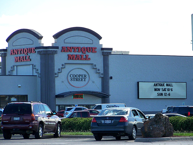 The exterior of Cooper Street Antique Mall, featuring prominent red signage, posted operating hours, and several cars parked out front.