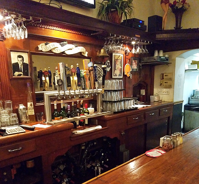 The bar area gleams with promise – wine glasses hanging like crystal stalactites above a wooden counter polished by decades of elbows.
