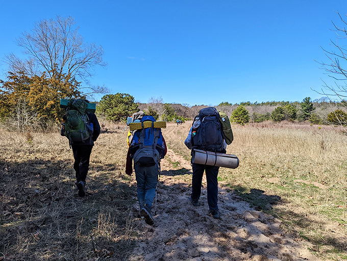 Three hikers venture into sandy terrain with everything they need on their backs. Modern-day explorers seeking wilderness therapy one step at a time.