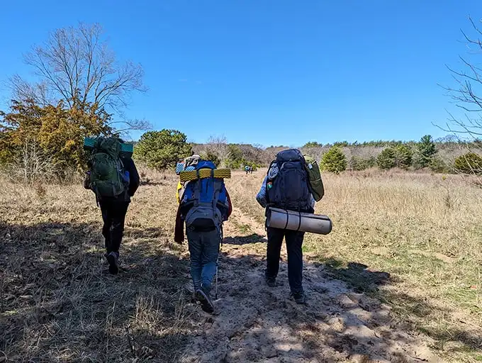 Three hikers venture into sandy terrain with everything they need on their backs. Modern-day explorers seeking wilderness therapy one step at a time.