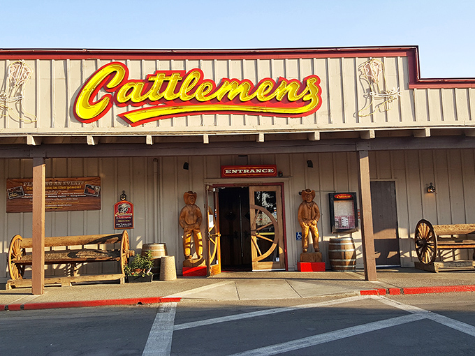 Wooden cowboys stand guard at Cattlemen's entrance, promising an authentic Western experience where the steaks match the decor's ambition.