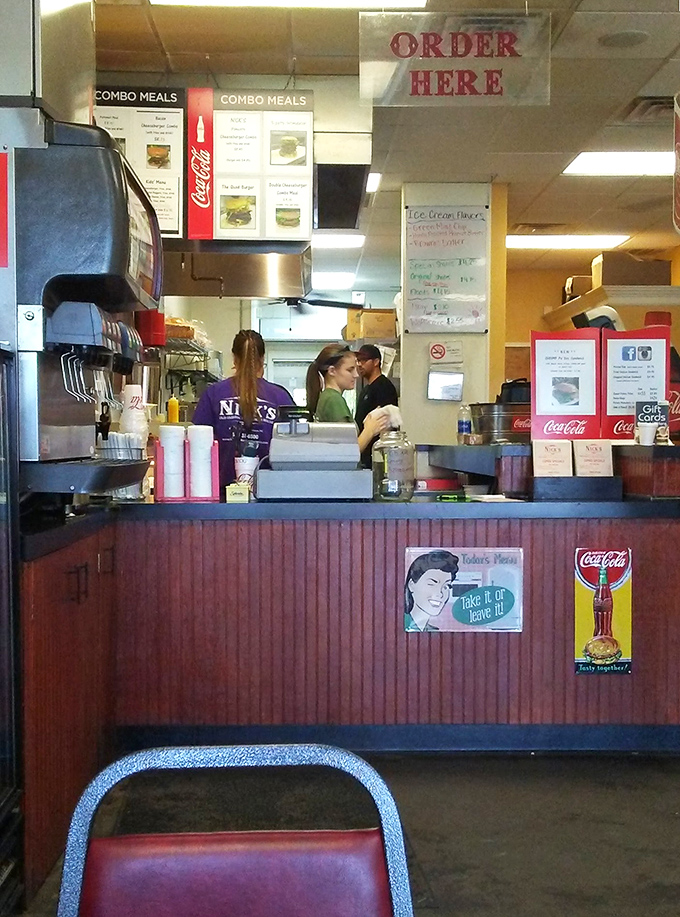 The ordering counter—where dreams become reality. Those vintage Coca-Cola signs aren't decoration; they're time machines to simpler days.