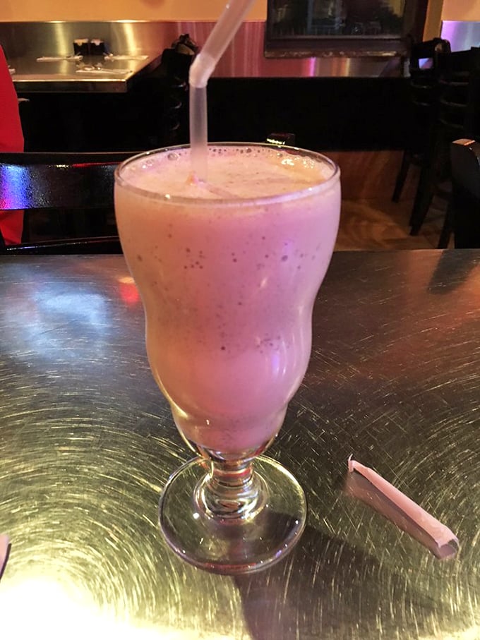 The milkshake arrives in its classic glass throne, pink and frothy, promising childhood nostalgia with grown-up indulgence.