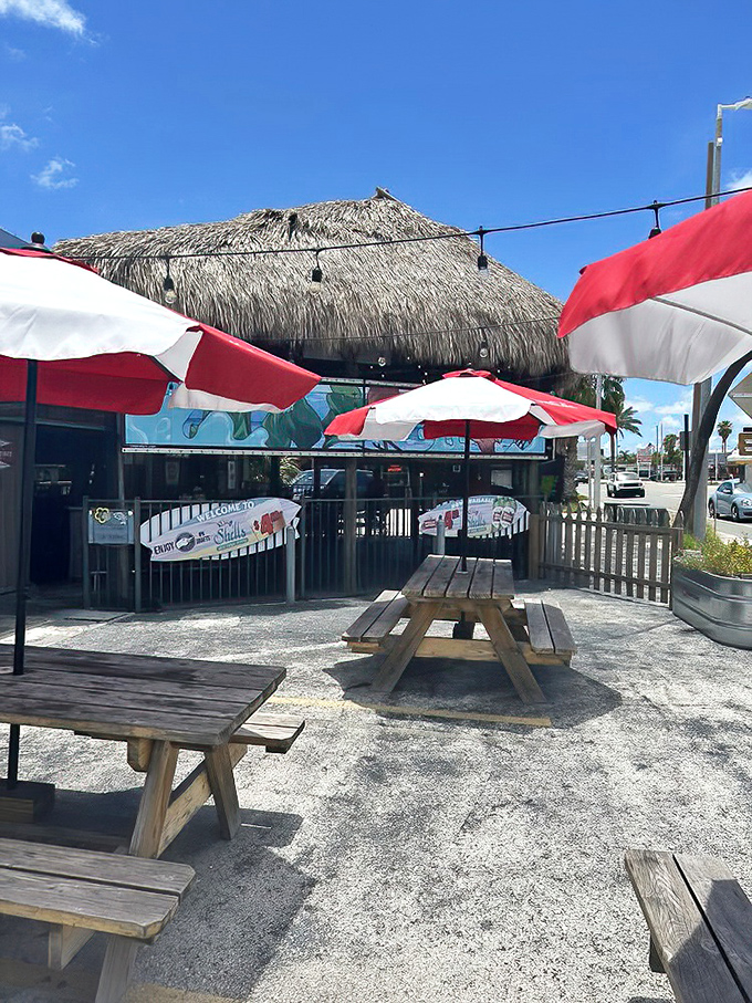 Red and white umbrellas shade wooden picnic tables on a sandy patch—because sometimes the best seafood comes with a side of Florida sunshine.