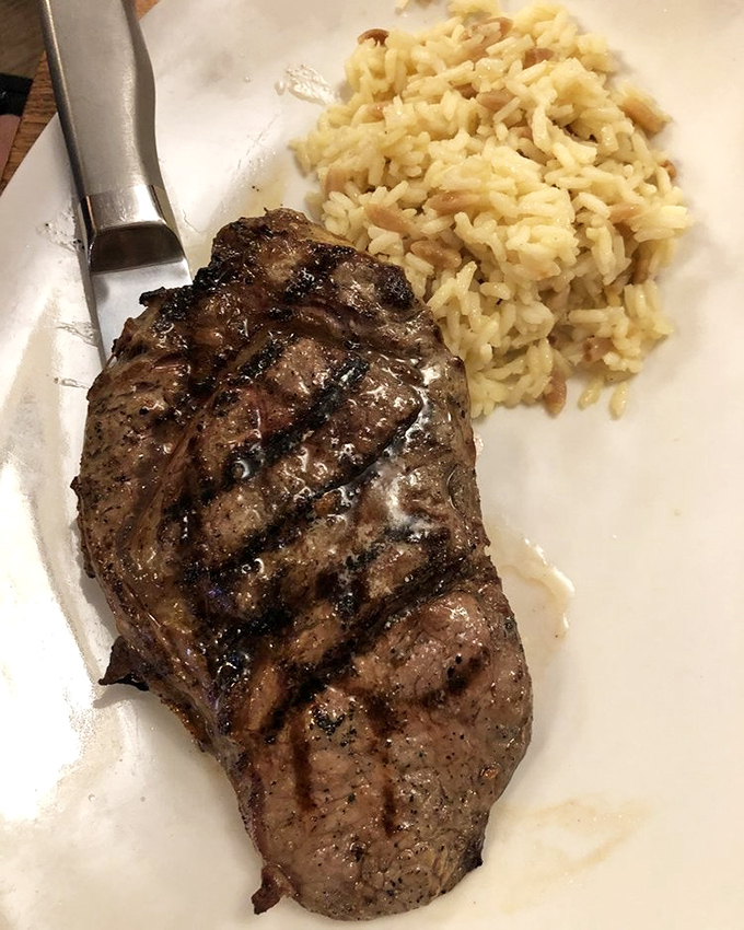 A ribeye with perfect grill marks lounging next to rice pilaf—it's the culinary equivalent of a power couple relaxing after conquering the world.