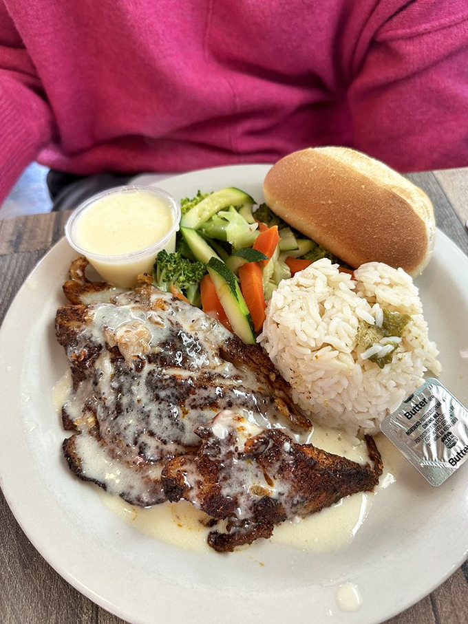 Blackened fish draped in creamy sauce alongside perfectly formed rice and fresh vegetables – a plate that balances indulgence with virtue.
