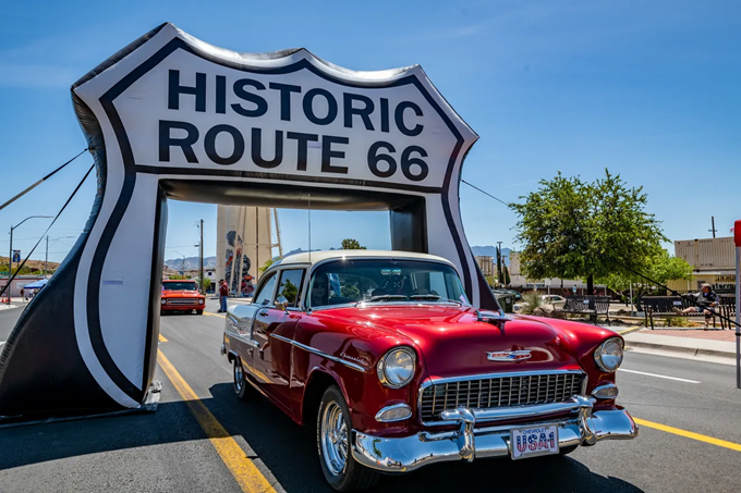 This gleaming Chevy passing under the Route 66 arch isn't just driving through a town—it's parading through a living museum of American road culture.