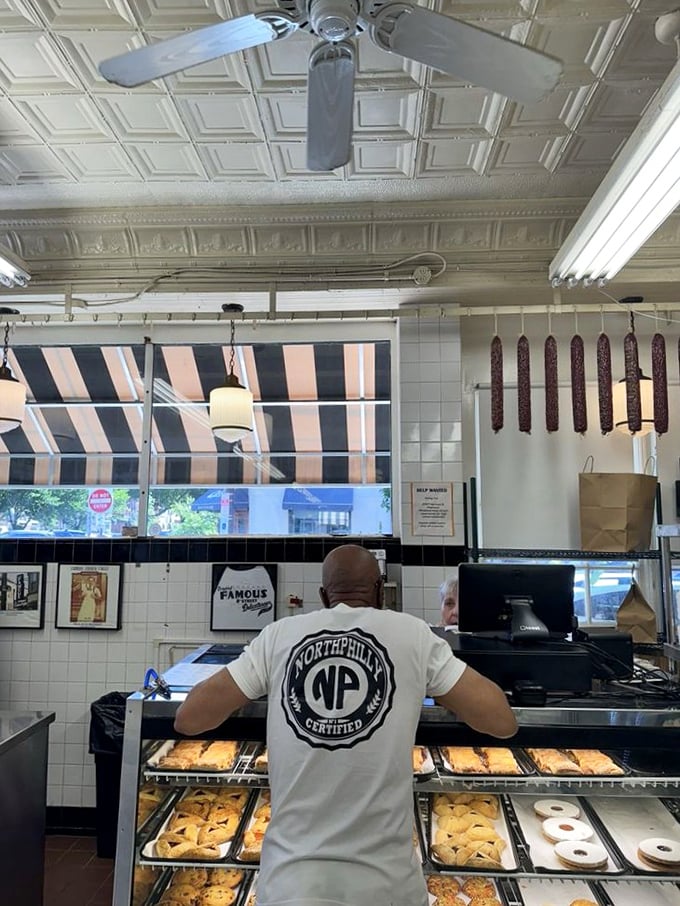 Behind the counter magic happens—where pastries tempt from below and salamis hang like delicious stalactites from a cave of culinary wonders.