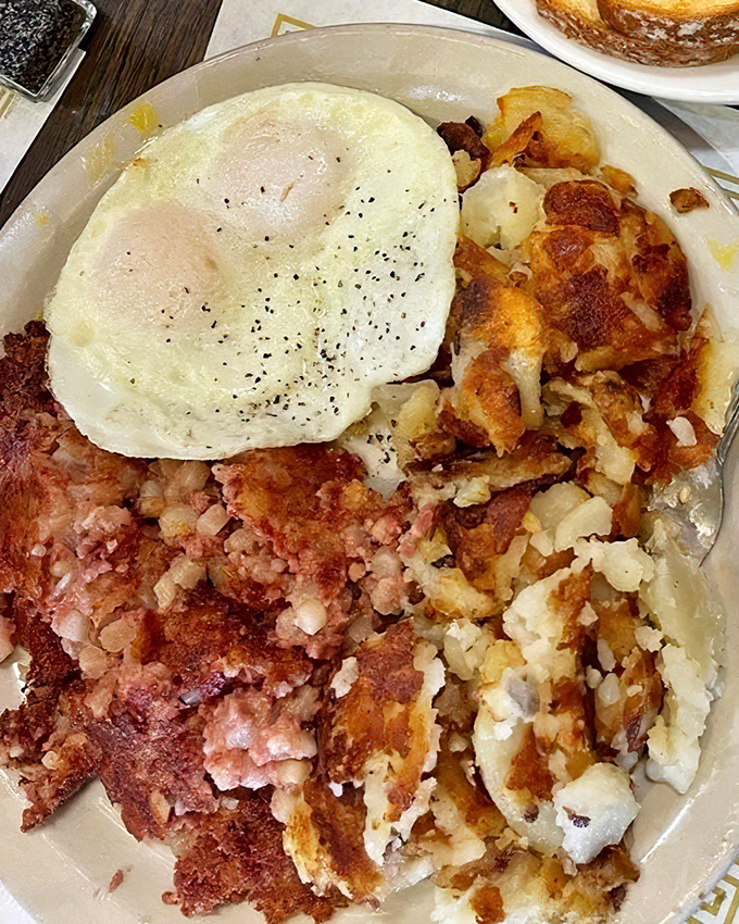A breakfast trinity: perfectly cooked egg, crispy corned beef hash, and golden potatoes – simple ingredients elevated through proper cooking technique.