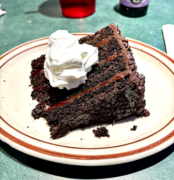 Chocolate cake that makes you reconsider your relationship with dessert. The whipped cream isn't decoration—it's a necessary cooling system for this decadence.