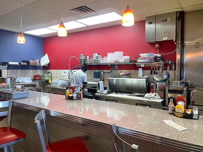 The open kitchen's red accent wall frames the morning's most important performance: breakfast made with speed, skill, and surprising grace.