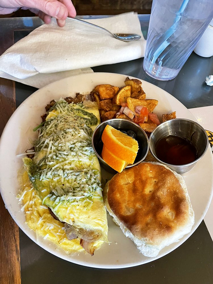 This omelet doesn't just sit on the plate—it commands attention with melted cheese, fresh sides, and a biscuit that's begging to be buttered.