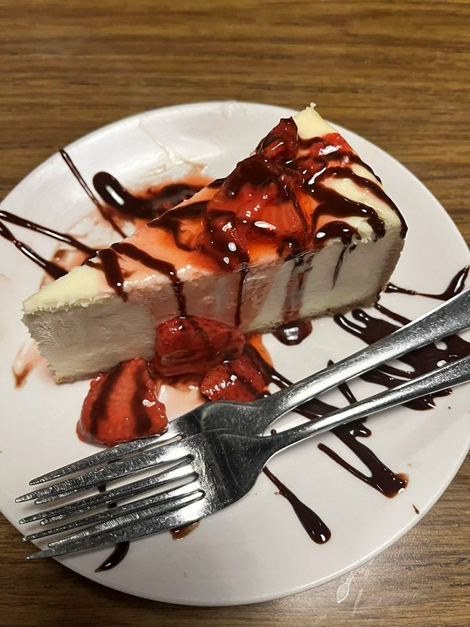 A slice of cheesecake that strikes the perfect balance between dense and light, adorned with strawberries and chocolate like jewelry on royalty.