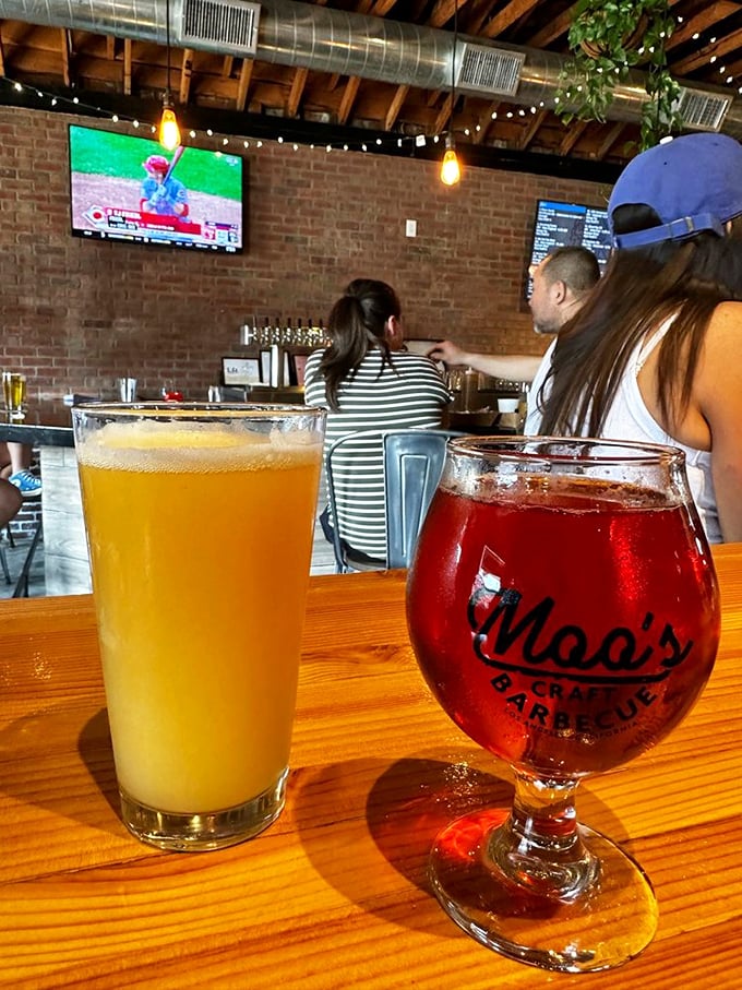 Craft beers in their natural habitat—one golden, one ruby—waiting to wash down smoky bites while sports play silently overhead.