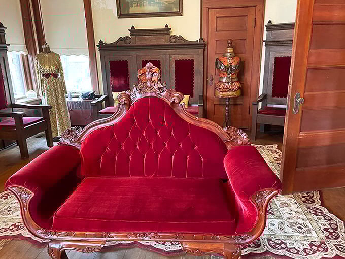 A crimson velvet loveseat fit for royalty—the kind of furniture that makes you sit up straighter and consider learning proper tea etiquette.