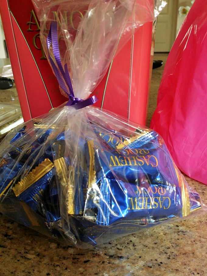 Gift bags of Cashew Roca tied with purple ribbon – because sometimes saying "I care about you" requires chocolate ammunition.