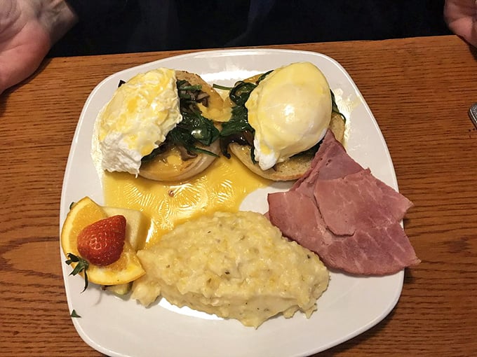 Eggs Benedict done right—perfectly poached eggs cascade golden yolk over English muffins, with grits and ham completing this Southern breakfast symphony.